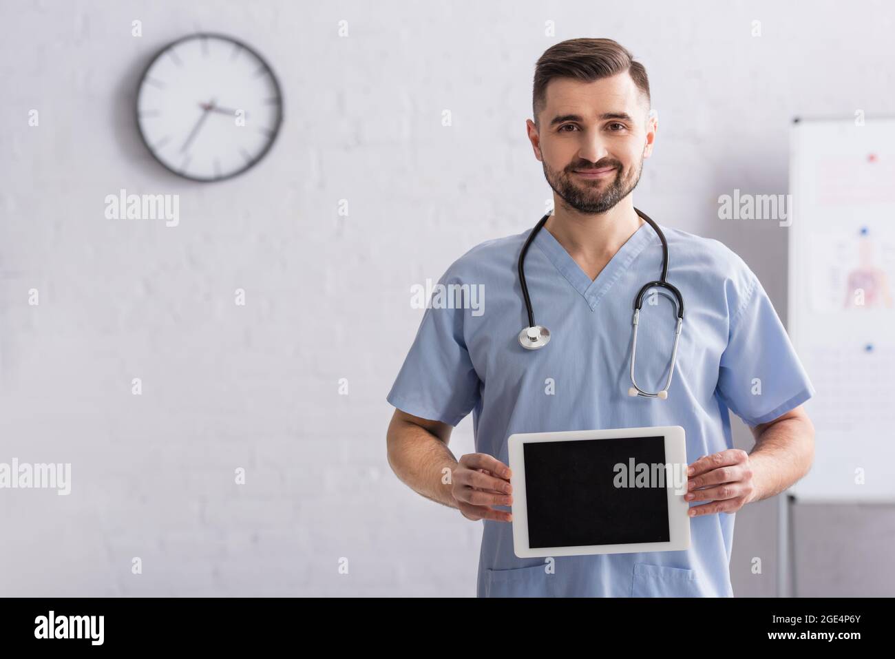 pleased doctor in blue uniform holding digital tablet with blank screen ...