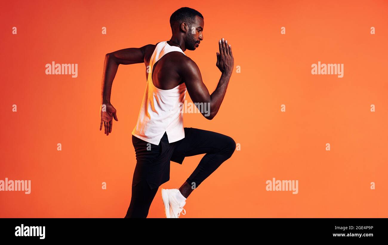Side view of a male runner sprinting over orange background Stock Photo ...