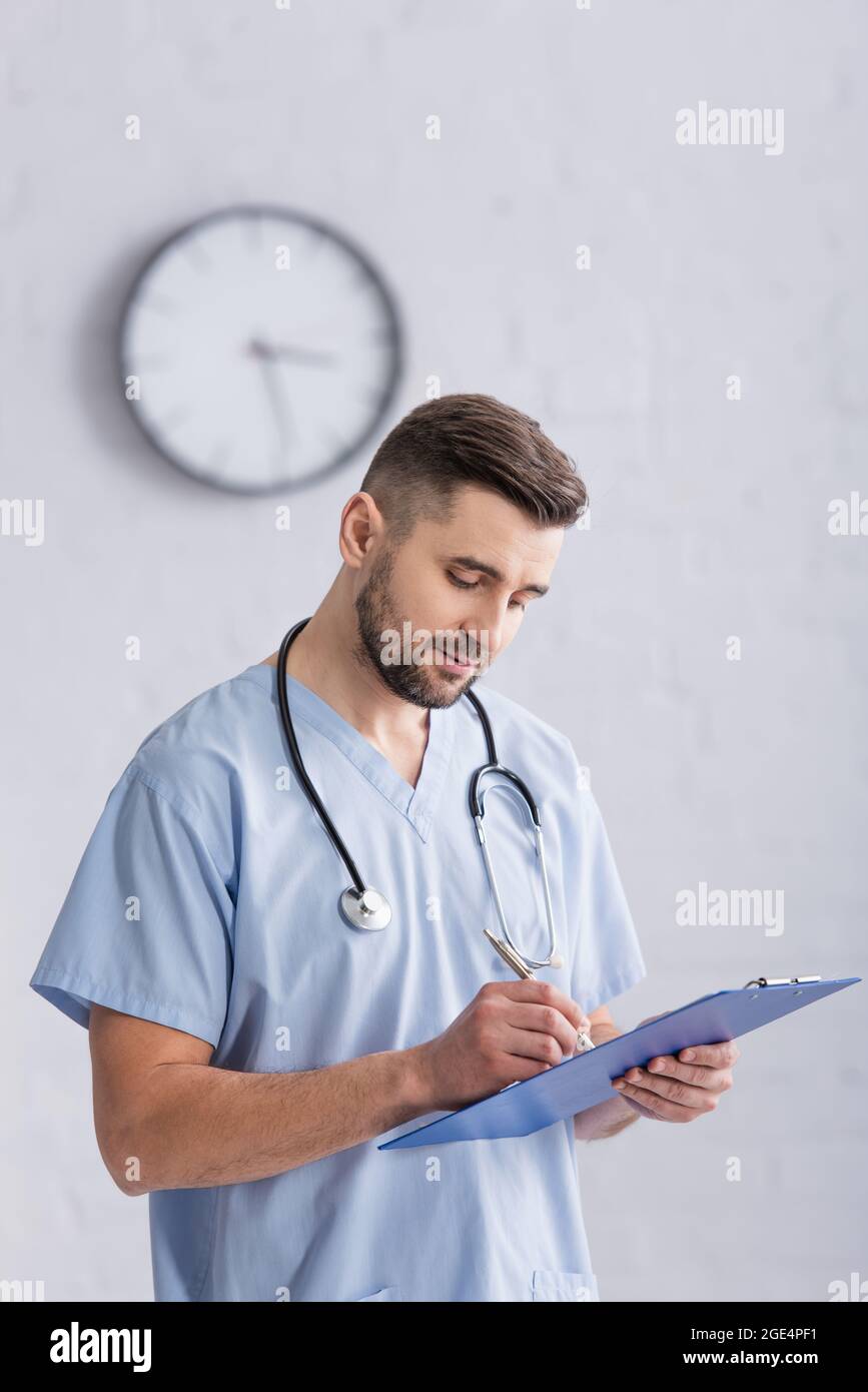 physician wearing blue uniform and stethoscope on neck writing ...