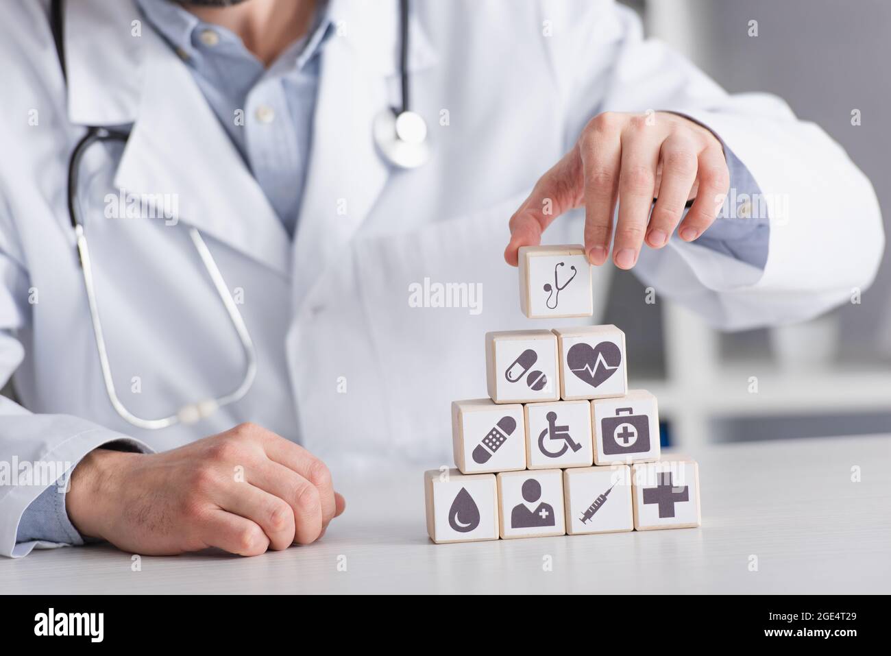 cropped view of blurred doctor in white coat making pyramid of cubes ...