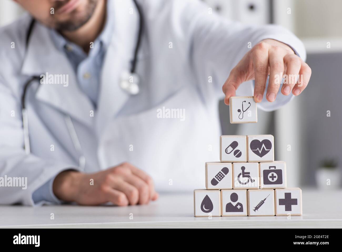 partial view of blurred physician arranging cubes with medical symbols ...