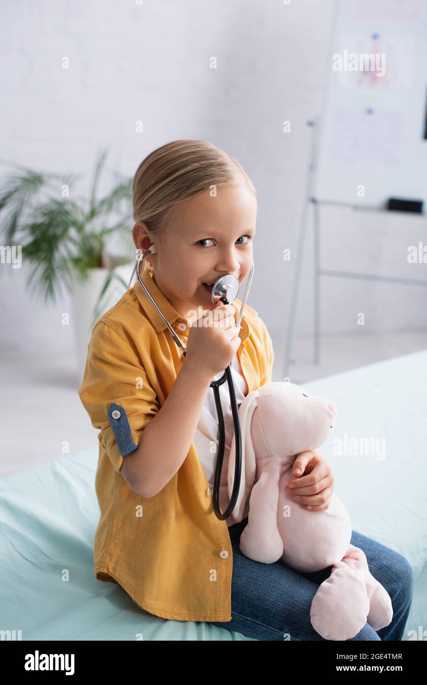 Smiling kid playing with soft toy and stethoscope on medical couch ...