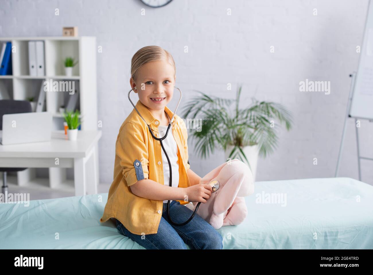 Smiling kid in stethoscope holding soft toy on medical couch Stock ...