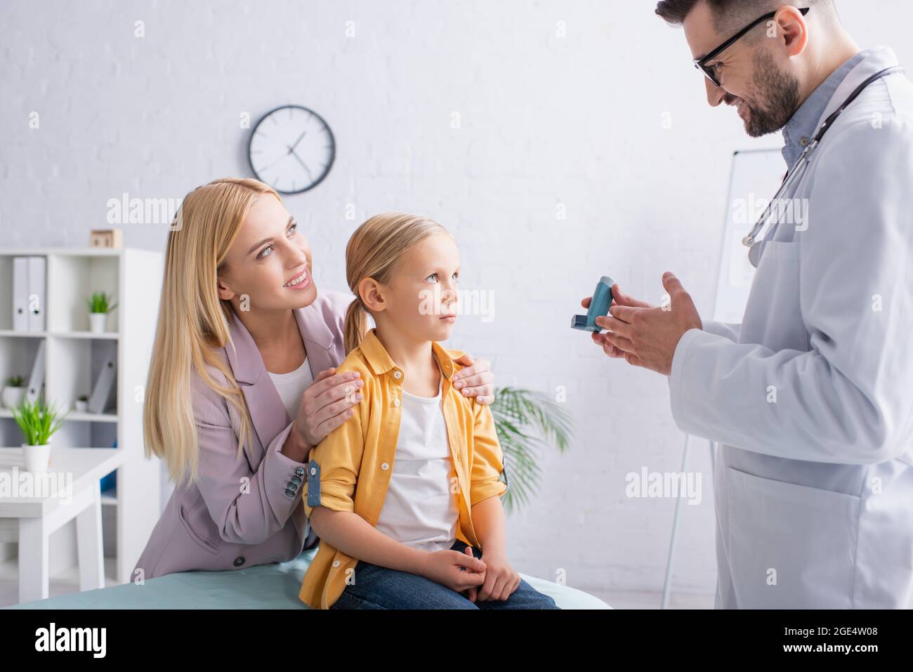 Smiling mother hugging child near family doctor with inhaler in clinic ...
