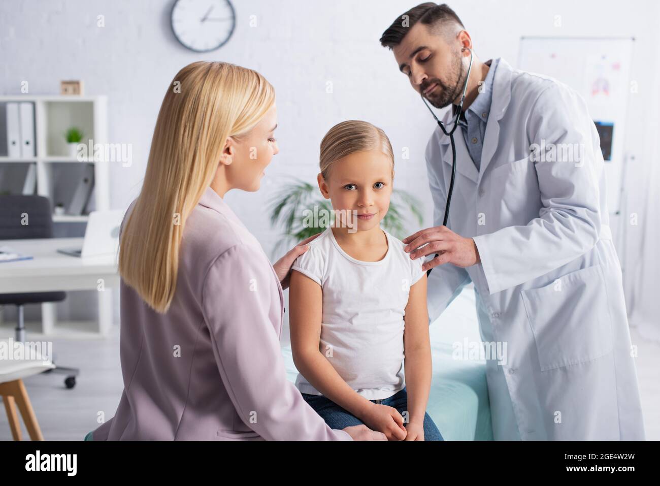 Mother looking at kid on medical couch near doctor with stethoscope ...
