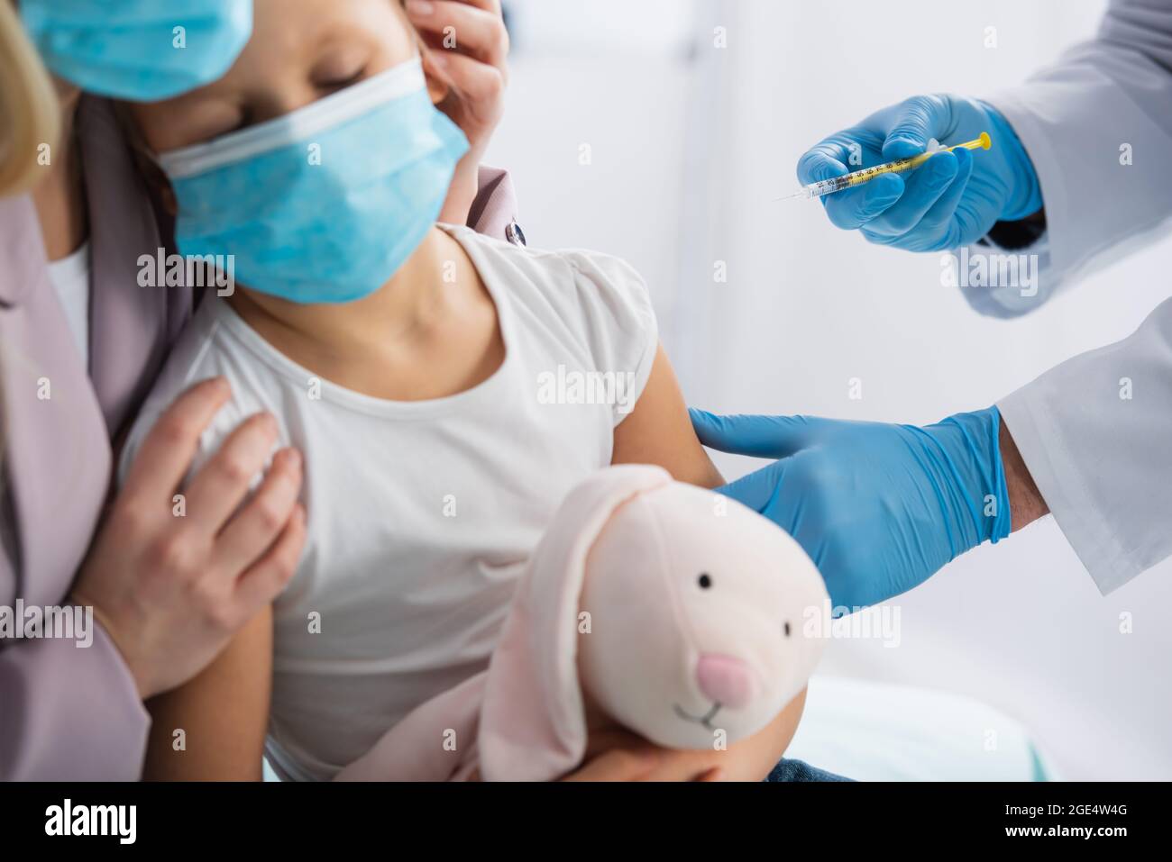 Doctor in latex gloves holding syringe near mother hugging kid in ...