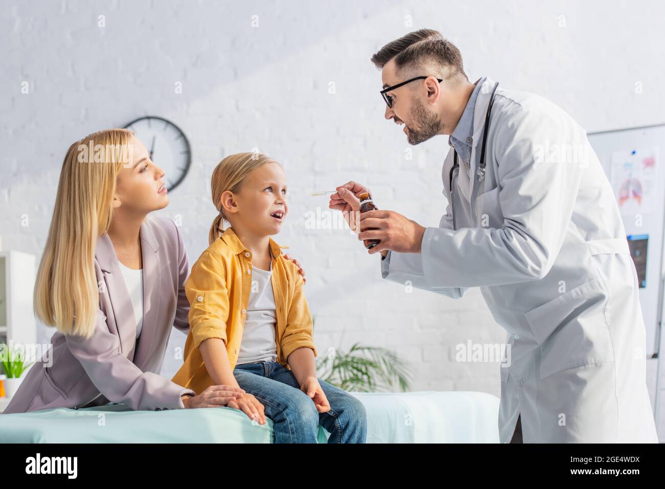 Doctor holding syrup near kid with open mouth and mother in clinic ...