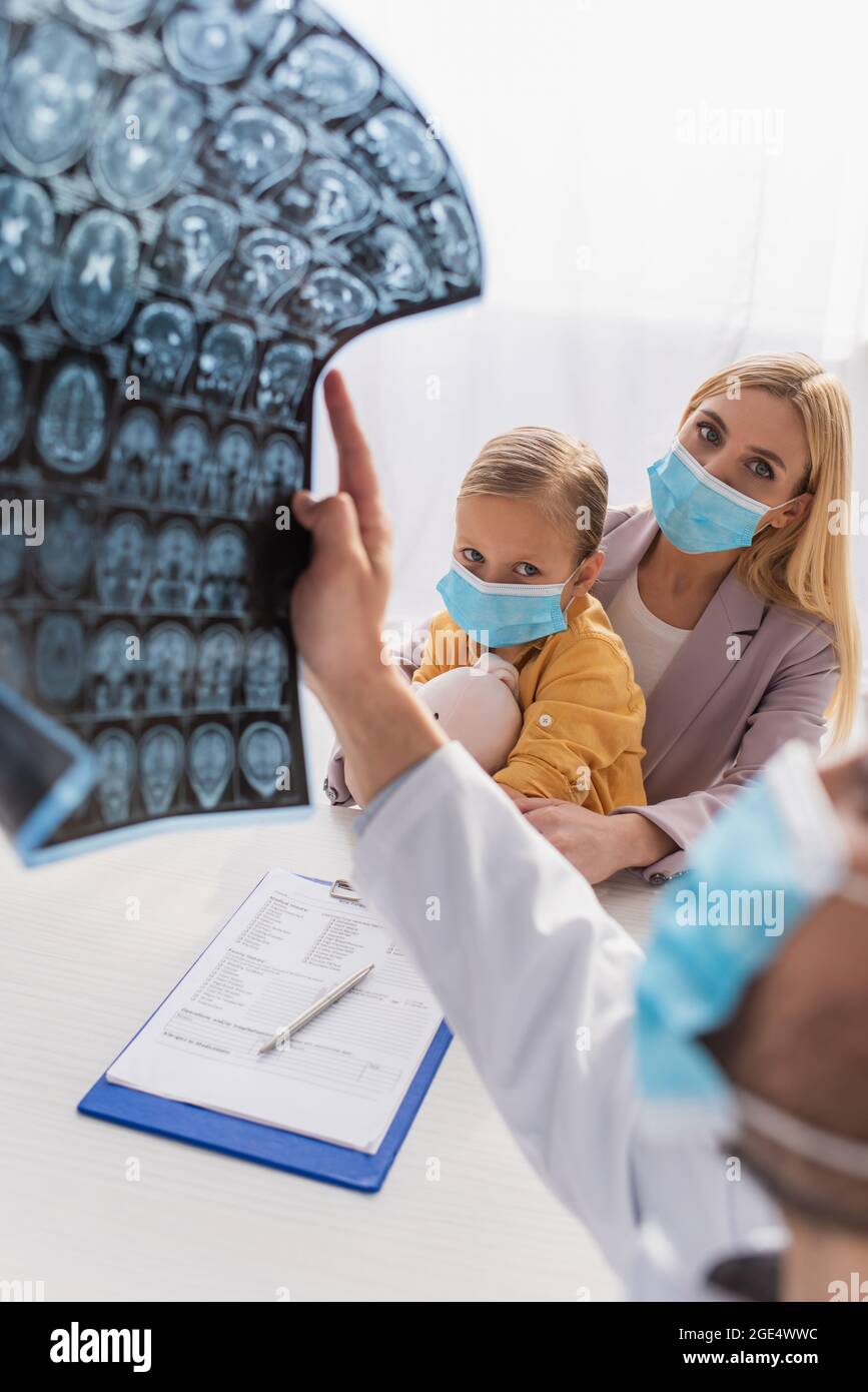 Mother and kid in medical masks looking at pediatrician with mri scan ...