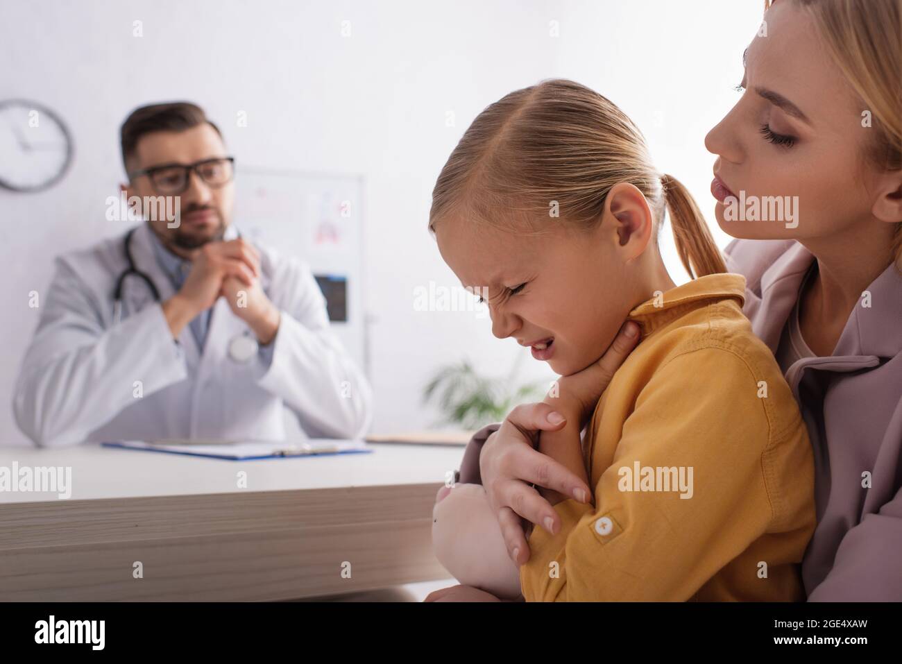 Diseased kid touching neck near mother and blurred pediatrician Stock ...