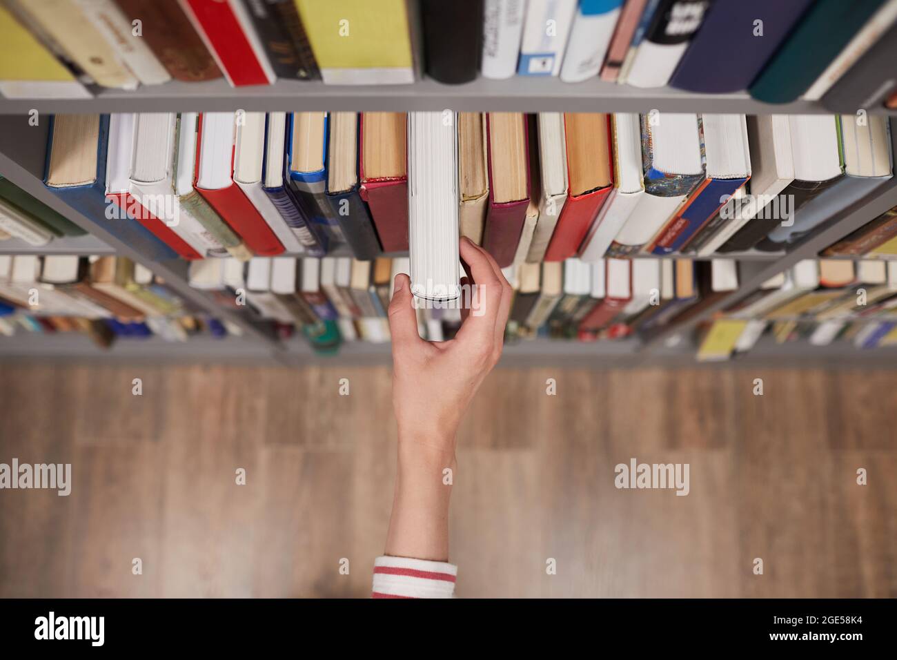 Top view close up of female hand taking book off shelf in library, copy ...