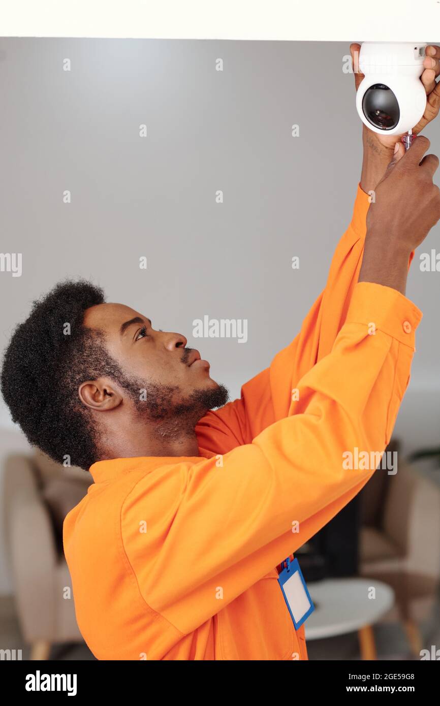 Serious young technician installing camera in apartment of customer ...
