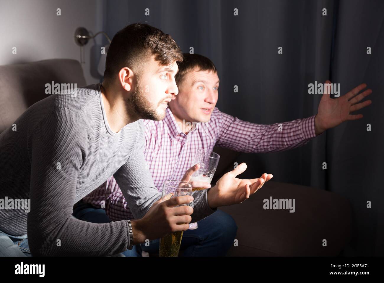 Two men watching tv with anxious uncertainty Stock Photo - Alamy