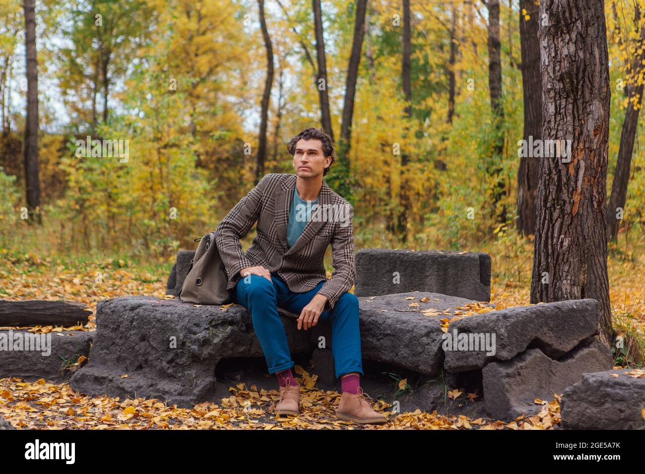 Tall handsome man dressed in a brown jacket posing with a bag on the ...
