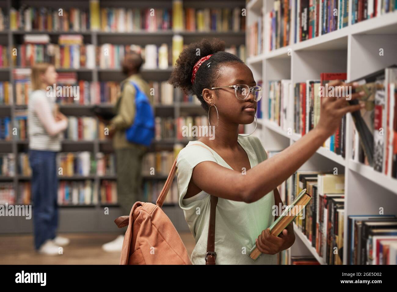 Waist up portrait of female Africa-American student choosing books in ...