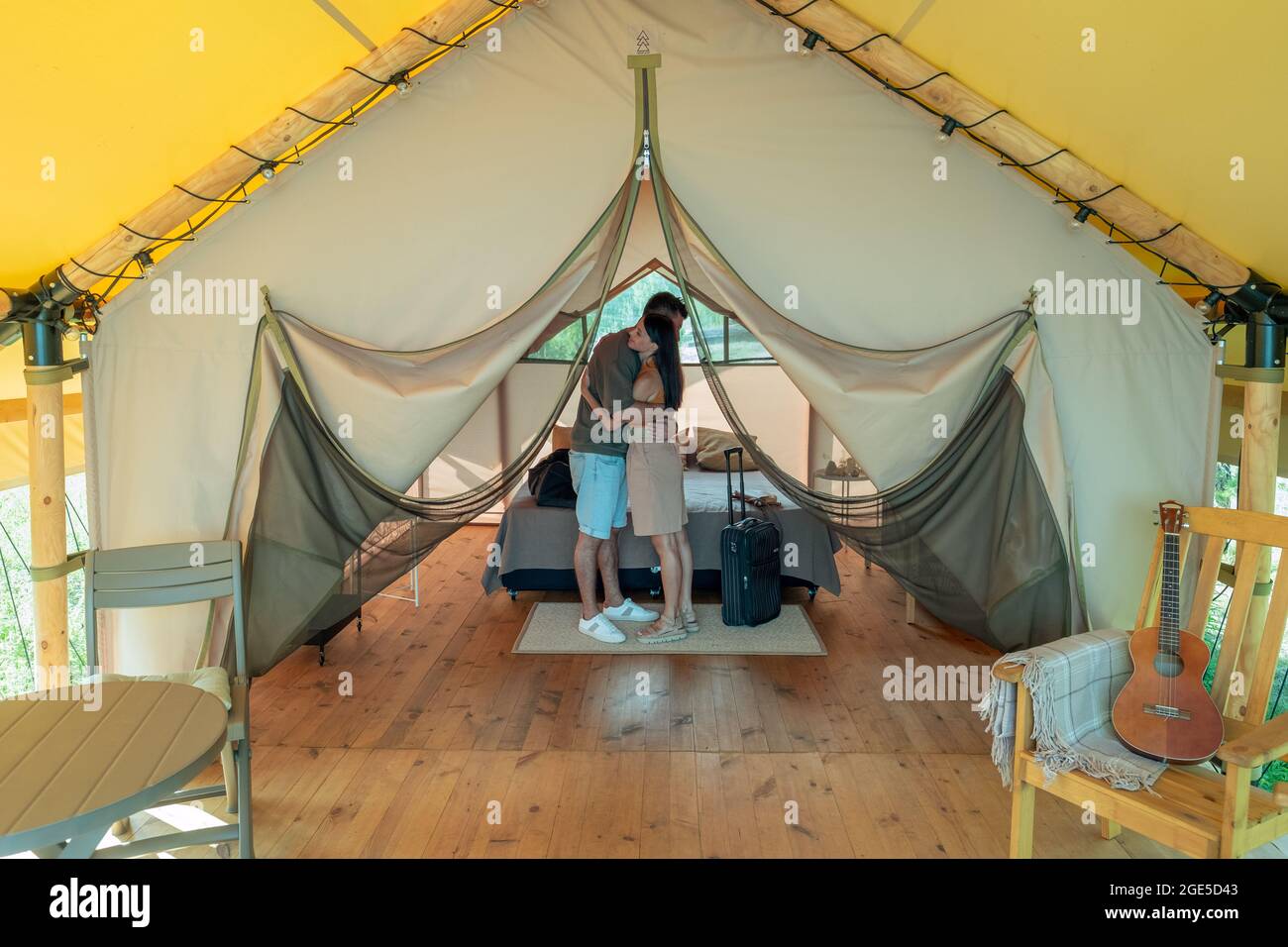 Young amorous couple standing in embrace by double bed inside glamping ...