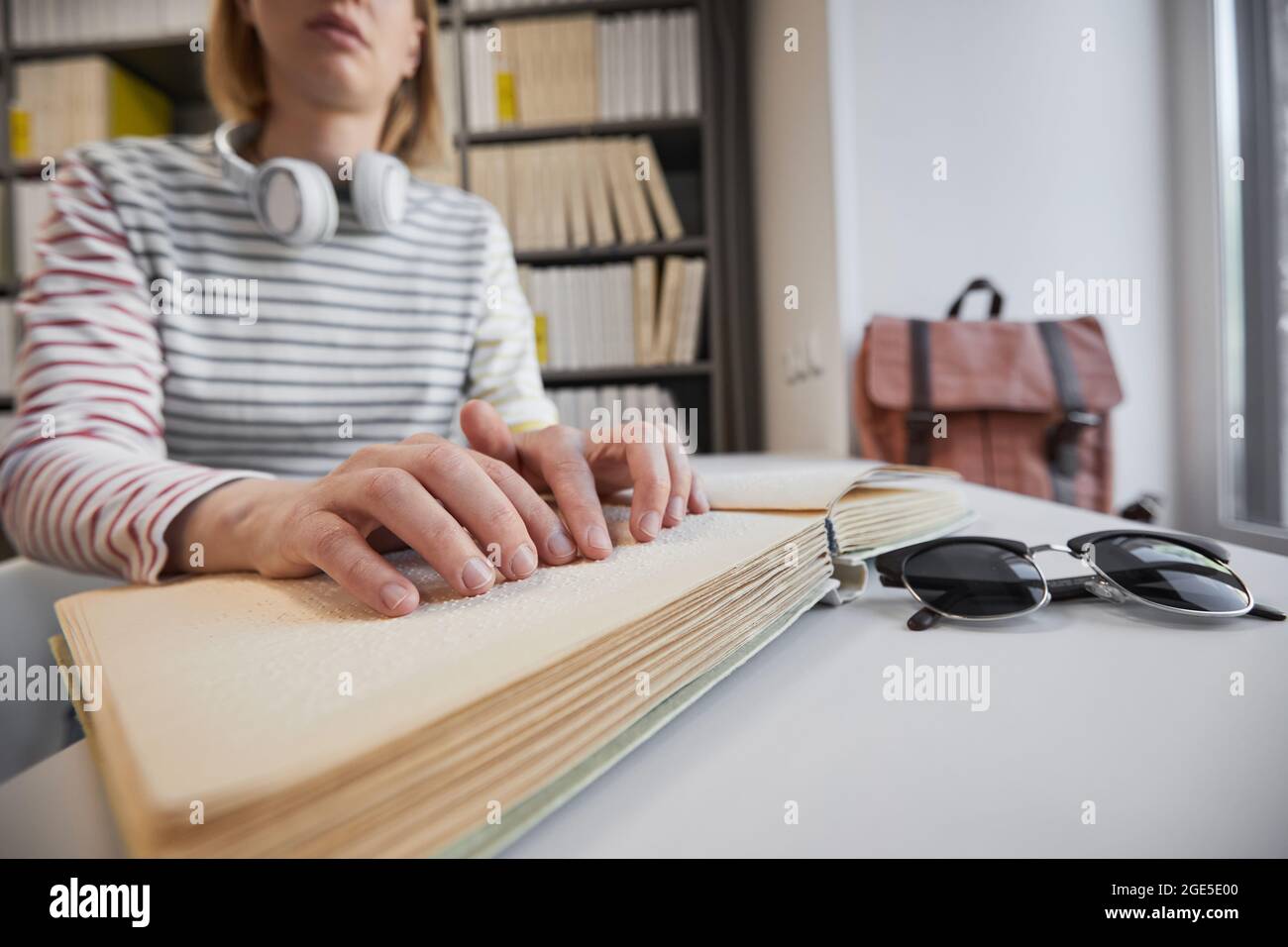Close up of young blind woman reading Braille book in college library ...