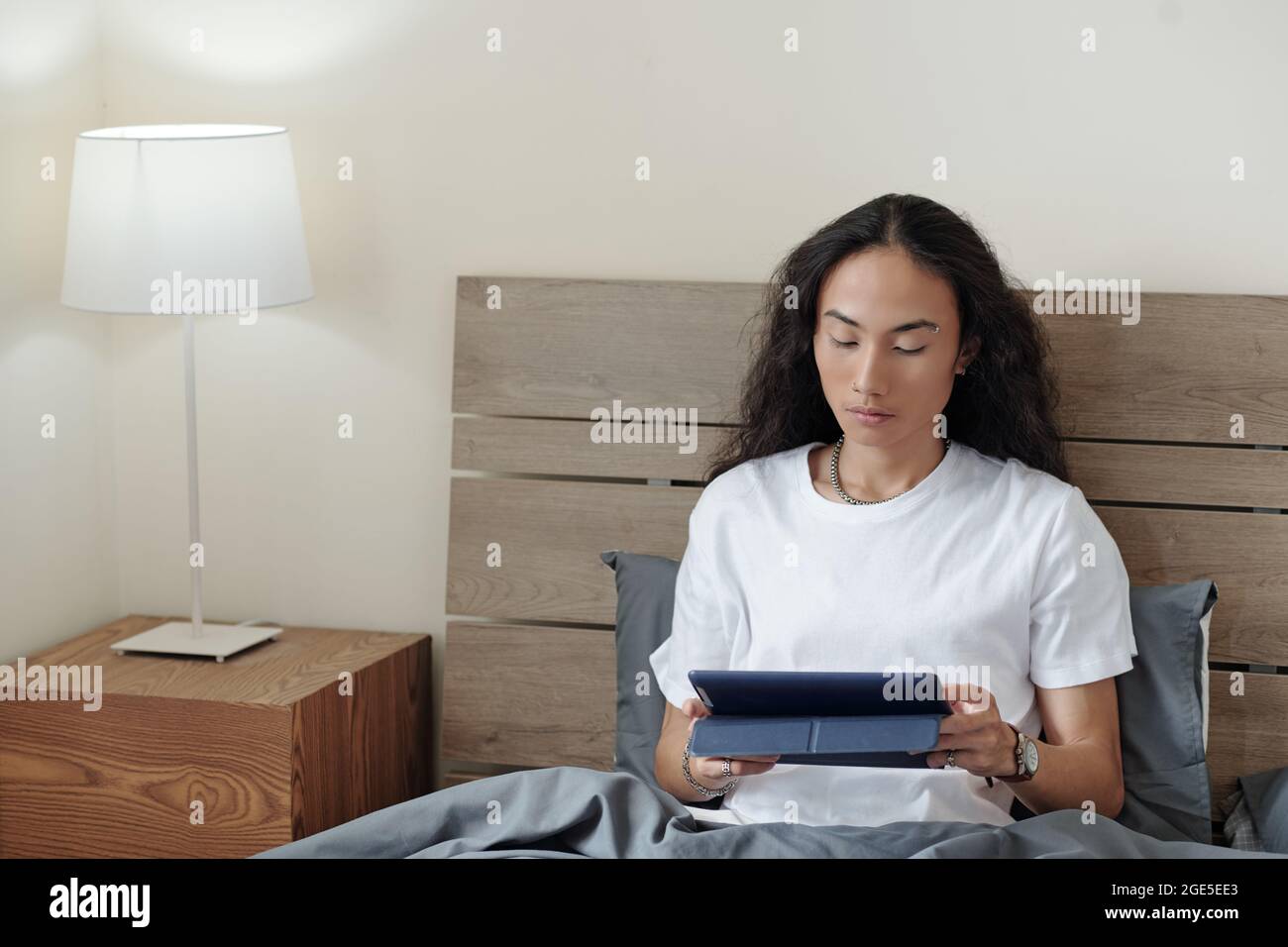 Pensive young man sitting in bed and watching new show episode on ...