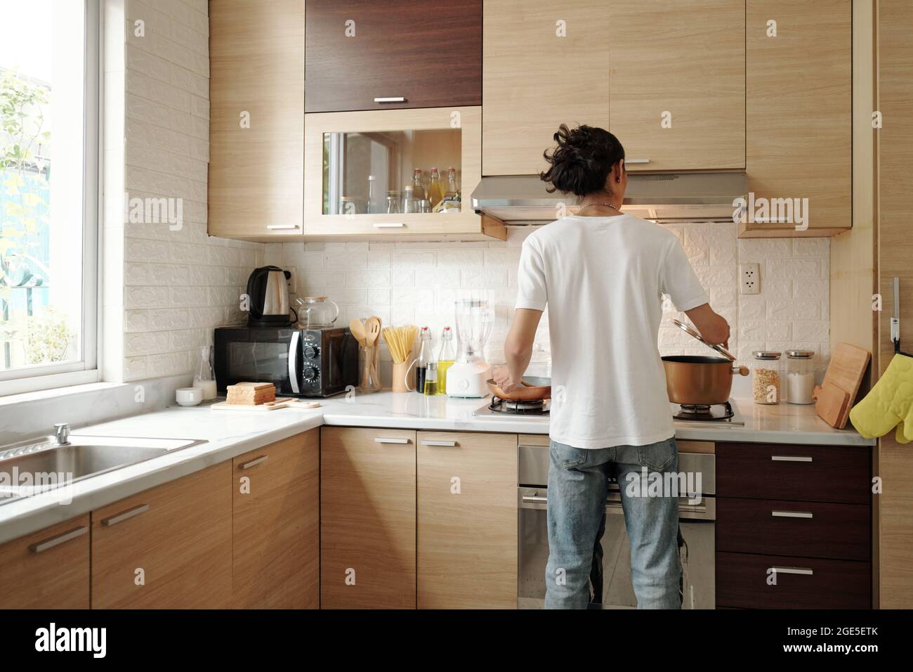 Young man in jeans and white shirt cooking dinner at kitchen counter ...