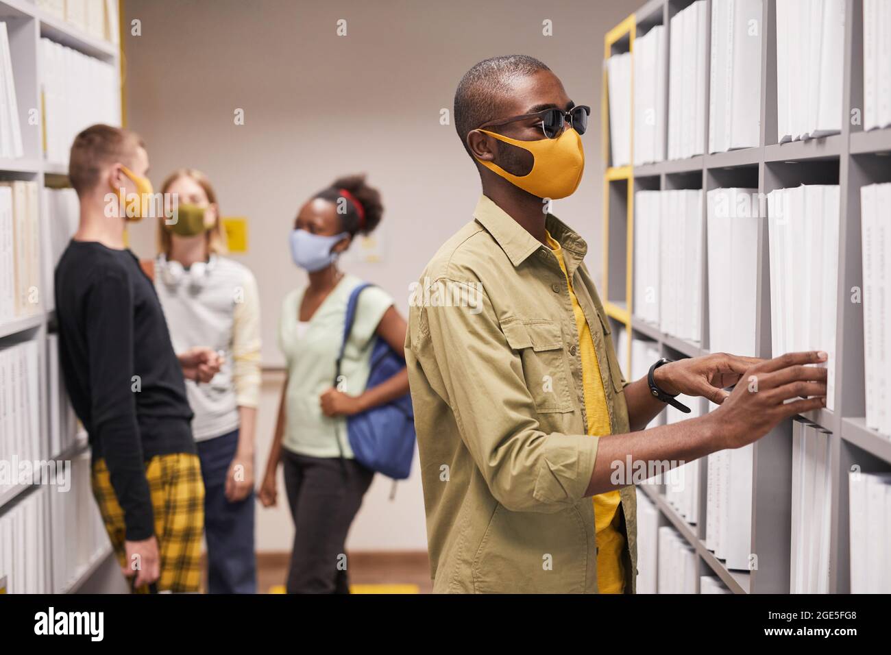 Portrait of blind African-American man wearing mask while choosing book ...