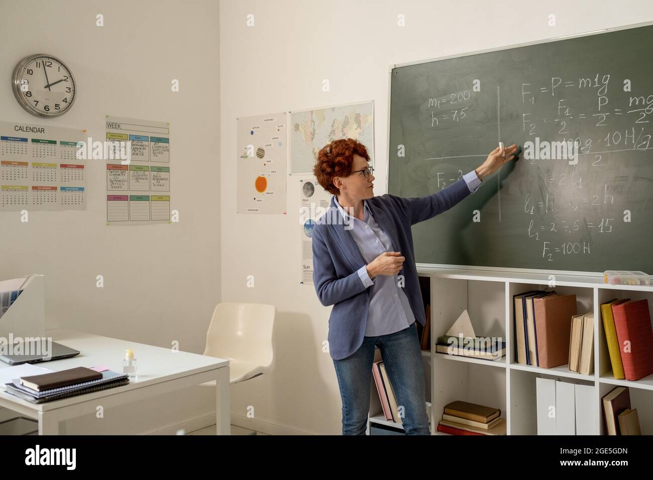 Young teacher of physics explaining formulas on blackboard at lesson ...