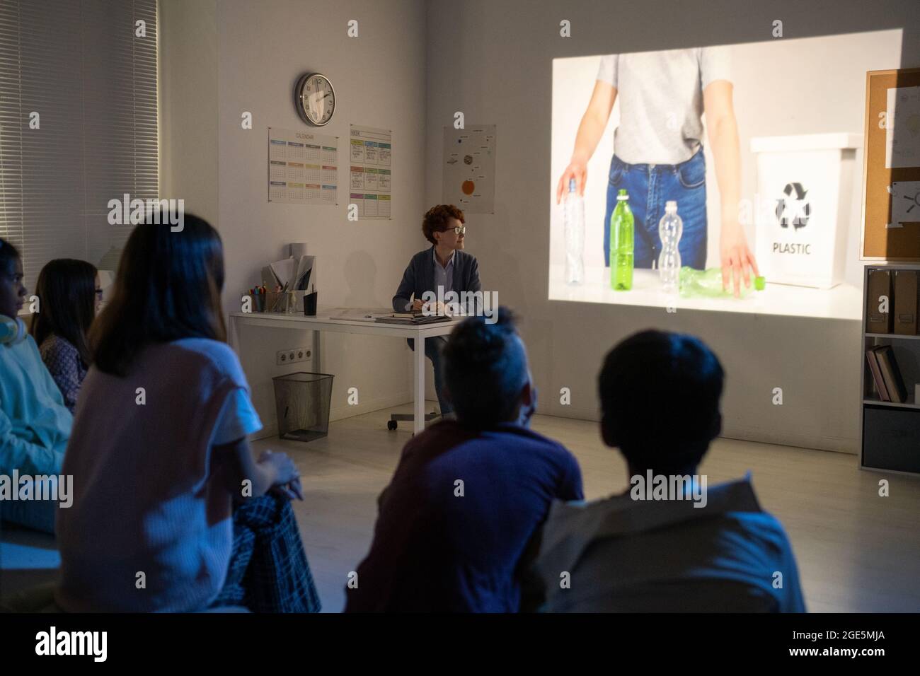 Schoolchildren watching video about recycling plastic bottles in dark ...