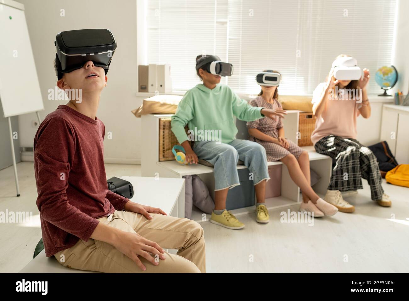 Contemporary schoolboy and his classmates in vr headsets watching video ...