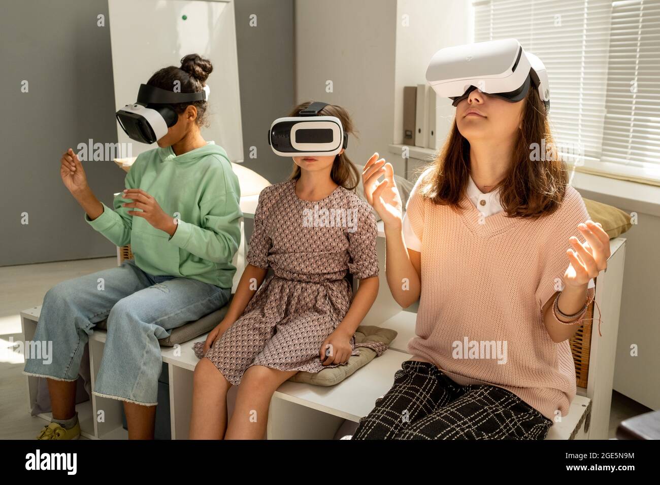 Three multiracial schoolgirls in vr headsets watching 3d presentation ...