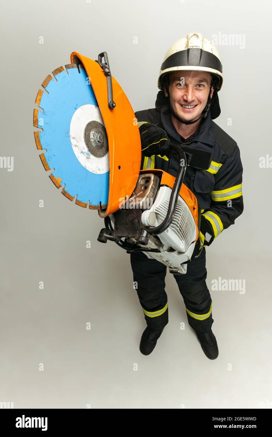 One smiling male firefighter dressed in uniform posing with saw over ...