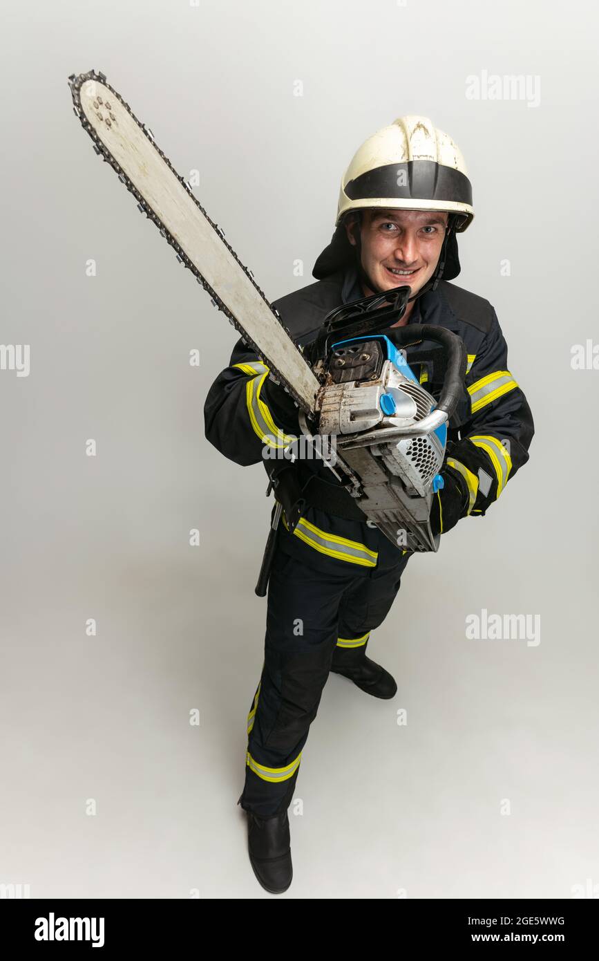 One smiling male firefighter dressed in uniform posing with saw over ...