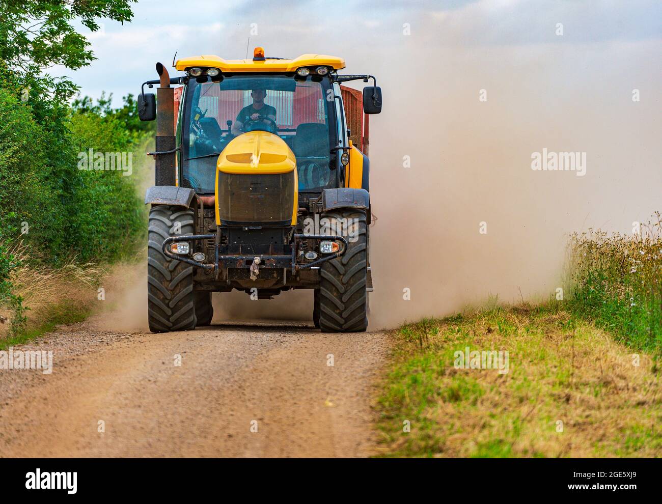 A yellow tractor towing a trailer speeding along a narrow farm track ...