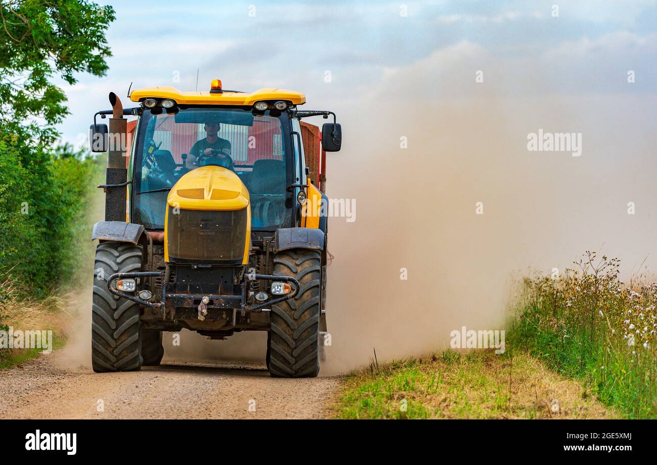 A yellow tractor towing a trailer speeding along a narrow farm track ...