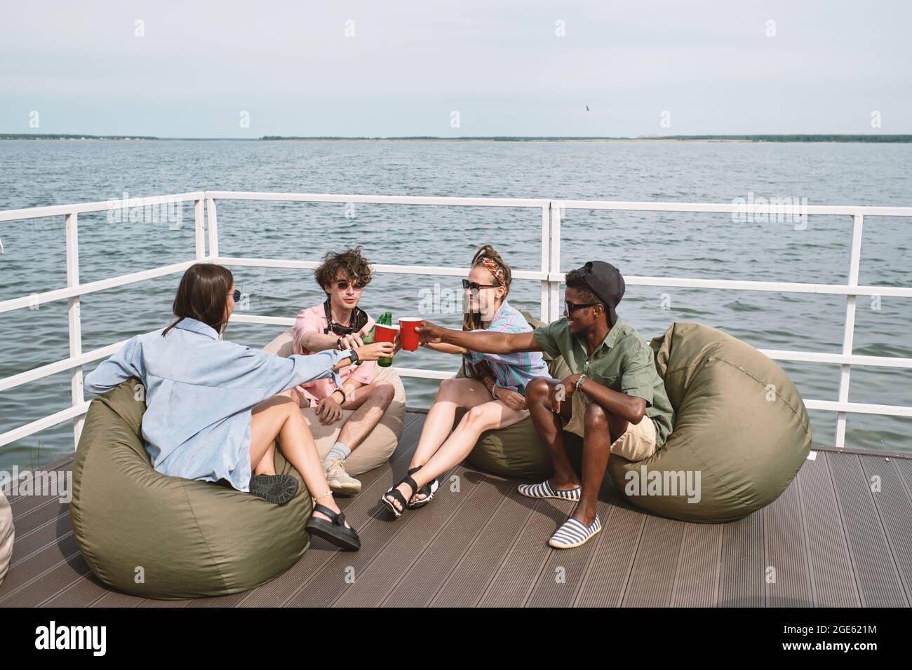 Group of young people having small party on wooden pier, they are ...