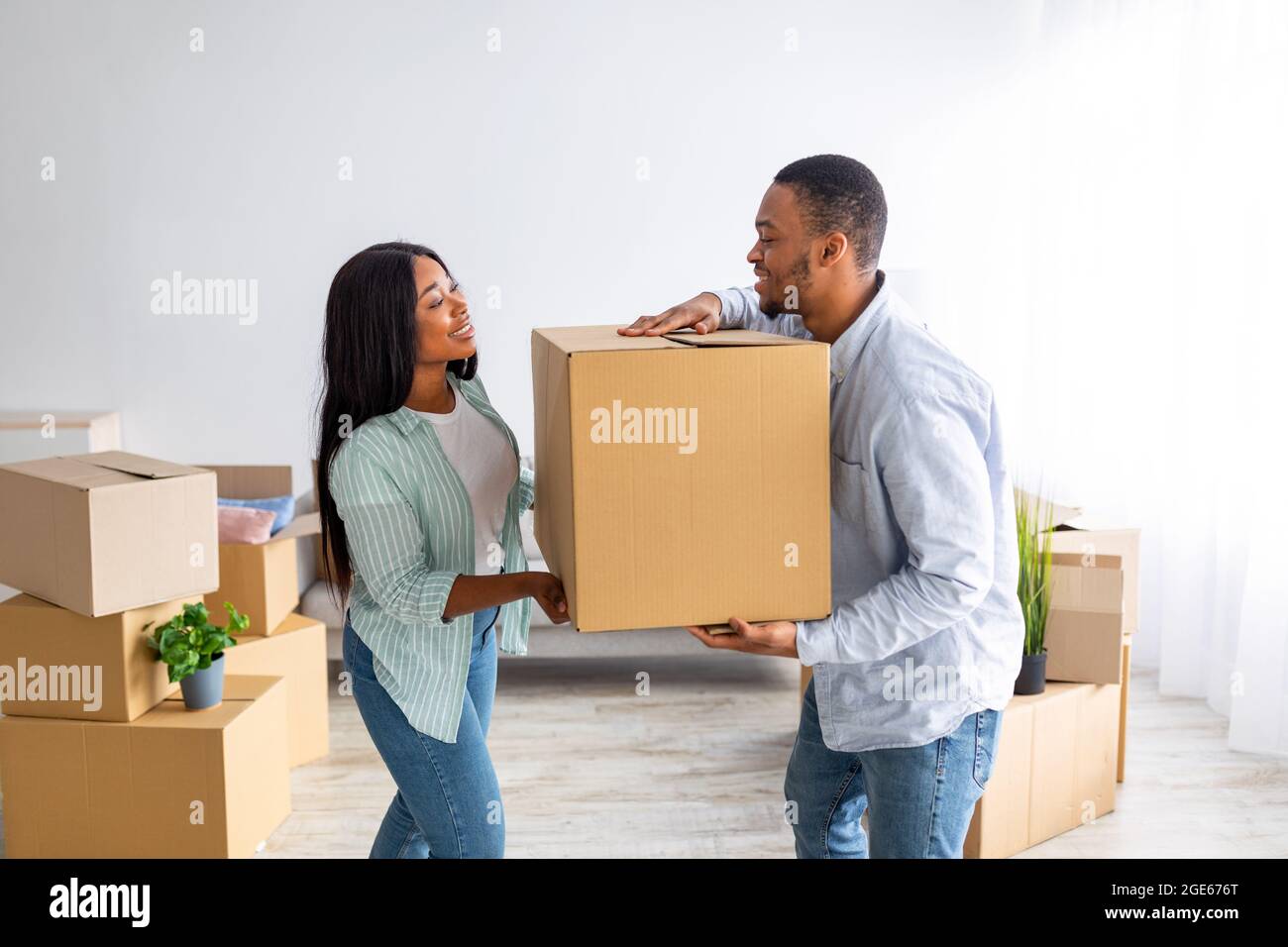 Happy young black couple carrying cardboard box together, helping each ...