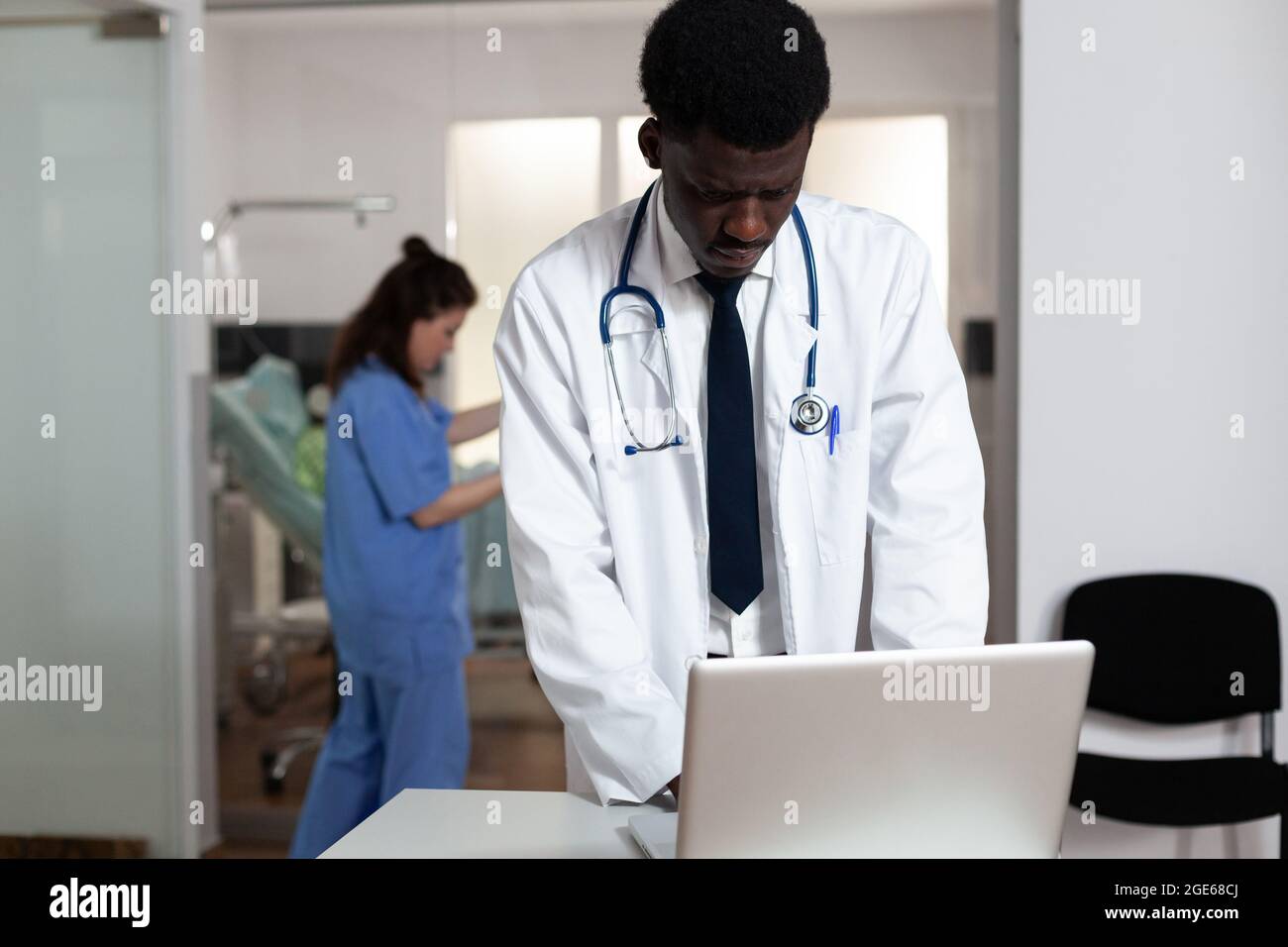 Portrait of african ethnicity doctor standing at desk with laptop in ...