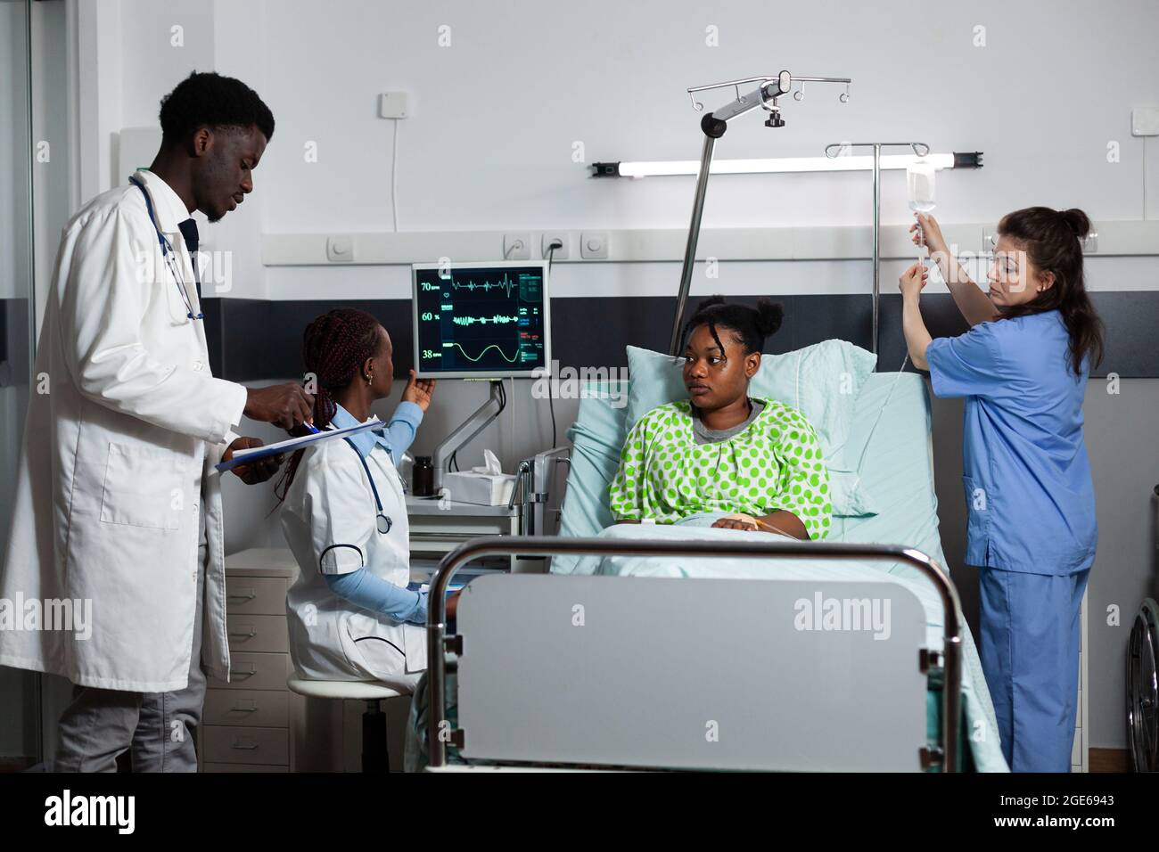 Multi ethnic medical team consulting young person in hospital ward bed ...