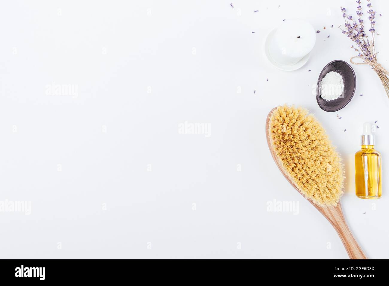 Organic body oil next to massage brush, lavender flowers and candle on ...