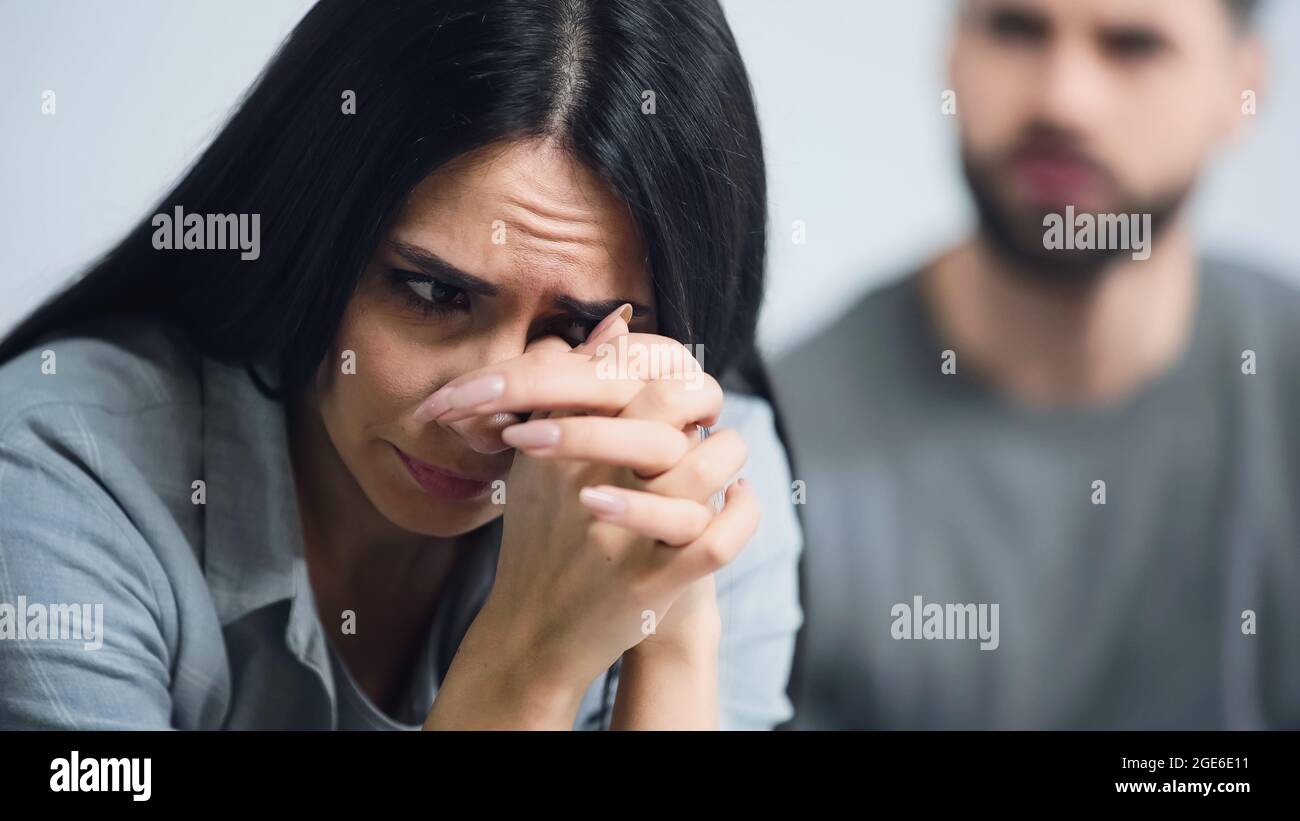 sad woman with clenched hands covering face while crying near blurred ...
