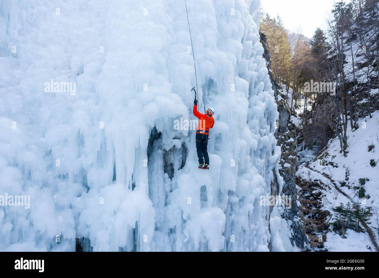 Aerial shot of a frozen ice waterfall, and the male climber progresses ...