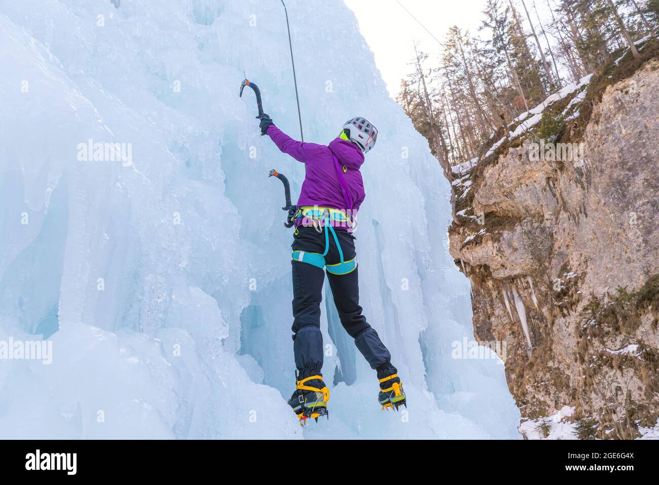 Female ice climber in traction position, swinging ice axes overhead and ...