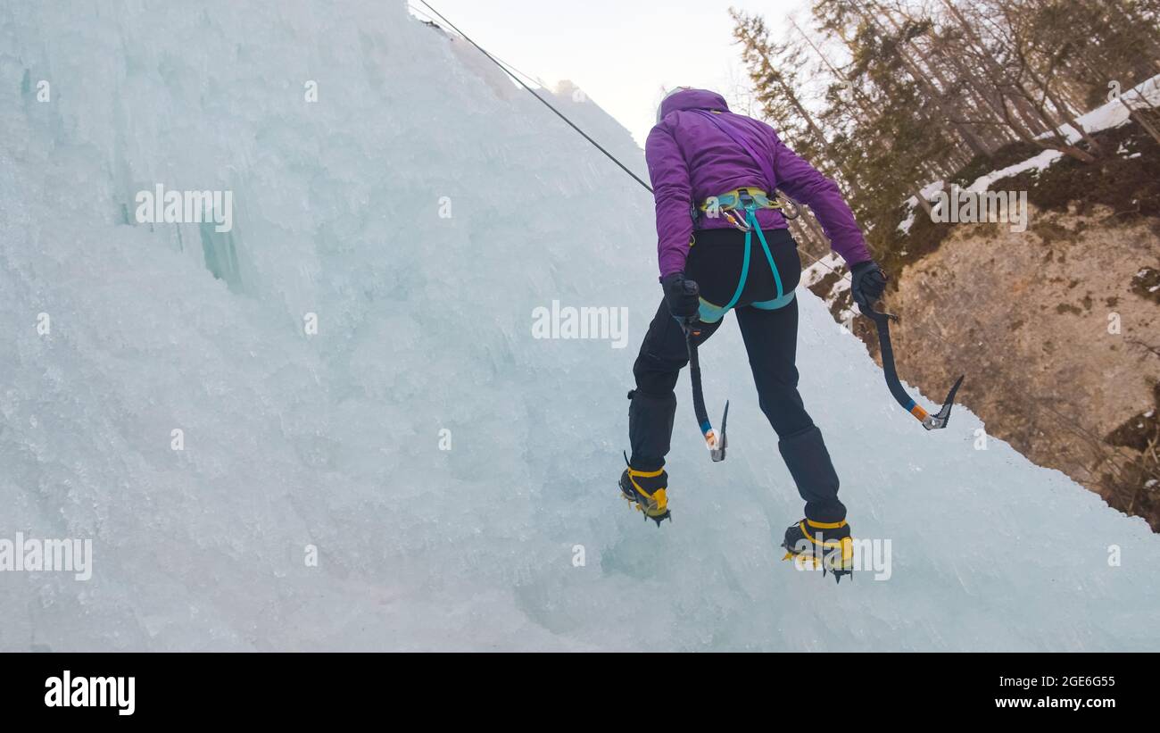 Female ice climber descending down an ice waterfall, stepping backward ...