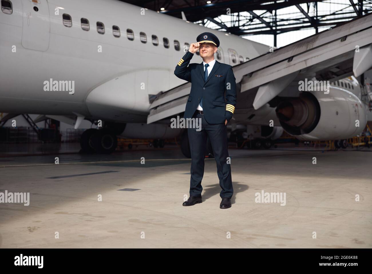 Full length shot of confident pilot in uniform looking away, adjusting ...