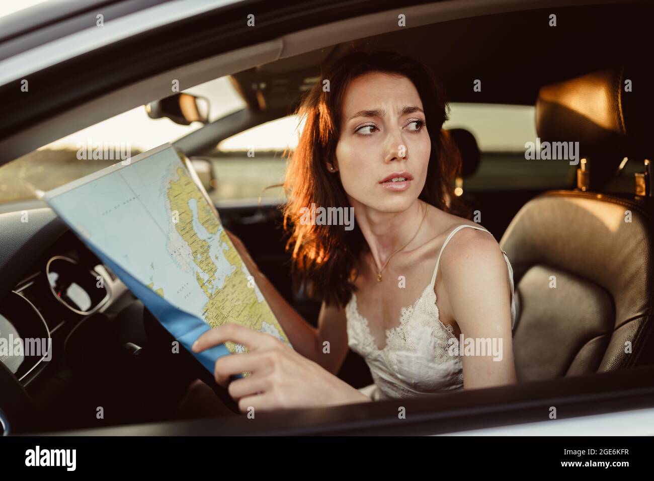 Lost young woman sitting in her car in the countryside and looking at ...