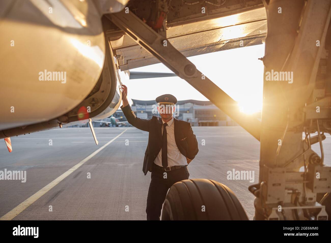 Professional male pilot in uniform and hat looking at camera, leaning ...