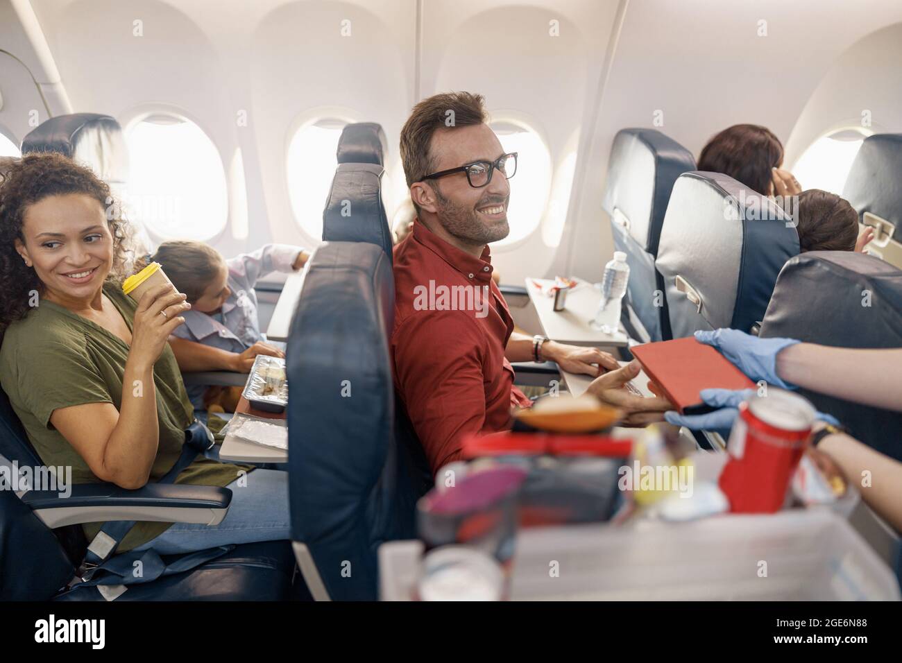 Happy passengers smiling while female flight attendant serving lunch on ...