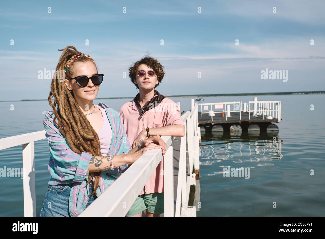 Positive fashionable young people standing on pier on lake posing for ...