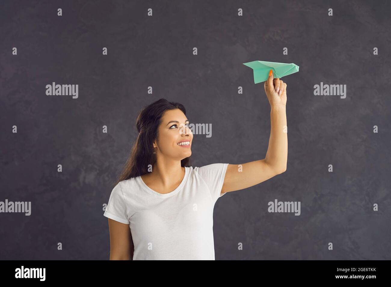 Portrait of a happy young woman holding a paper airplane in her hand ...