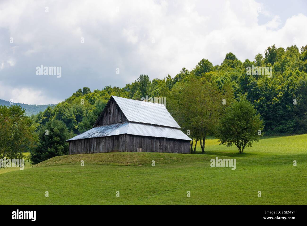 A barn sits on a hillside pasture with trees under cloudy skies in ...