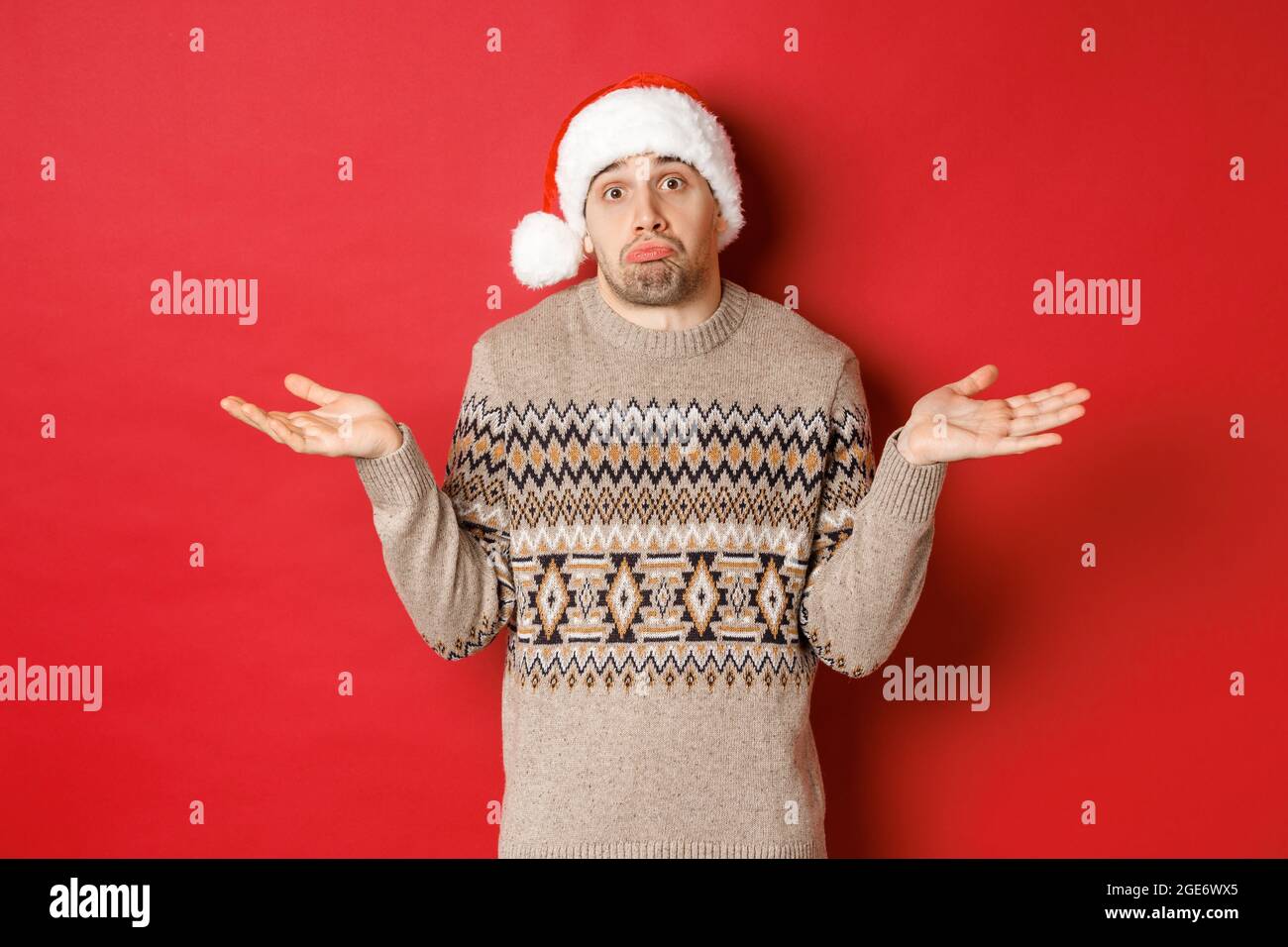 Image of clueless young man in sweater and santa hat, shrugging and ...