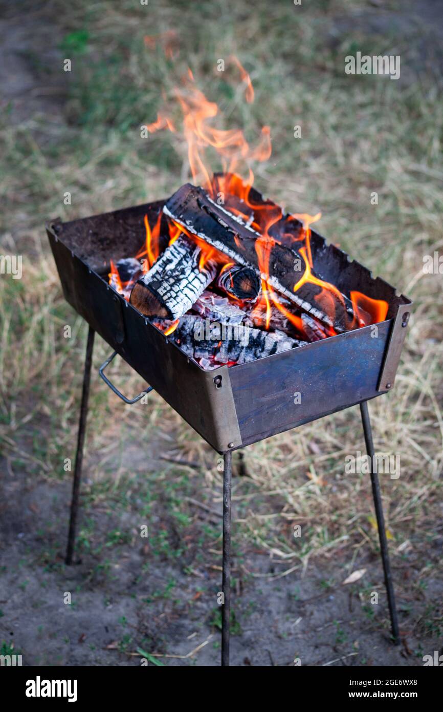 A small folding portable brazier filled with burning wood. Cooking on ...