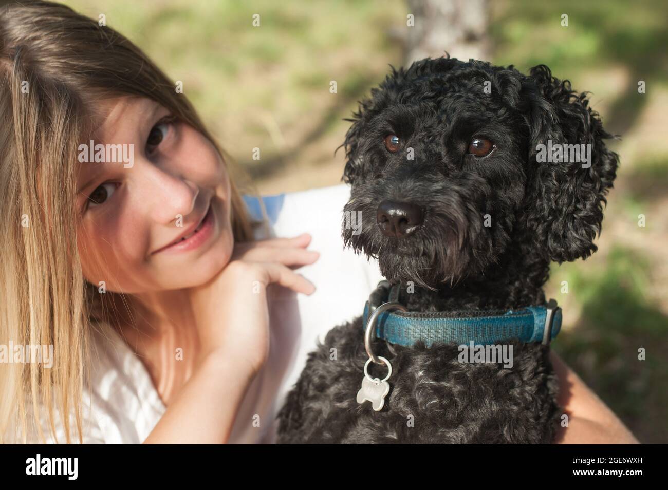 Cute smiling little girl playing with her dog, black poodle, in the ...